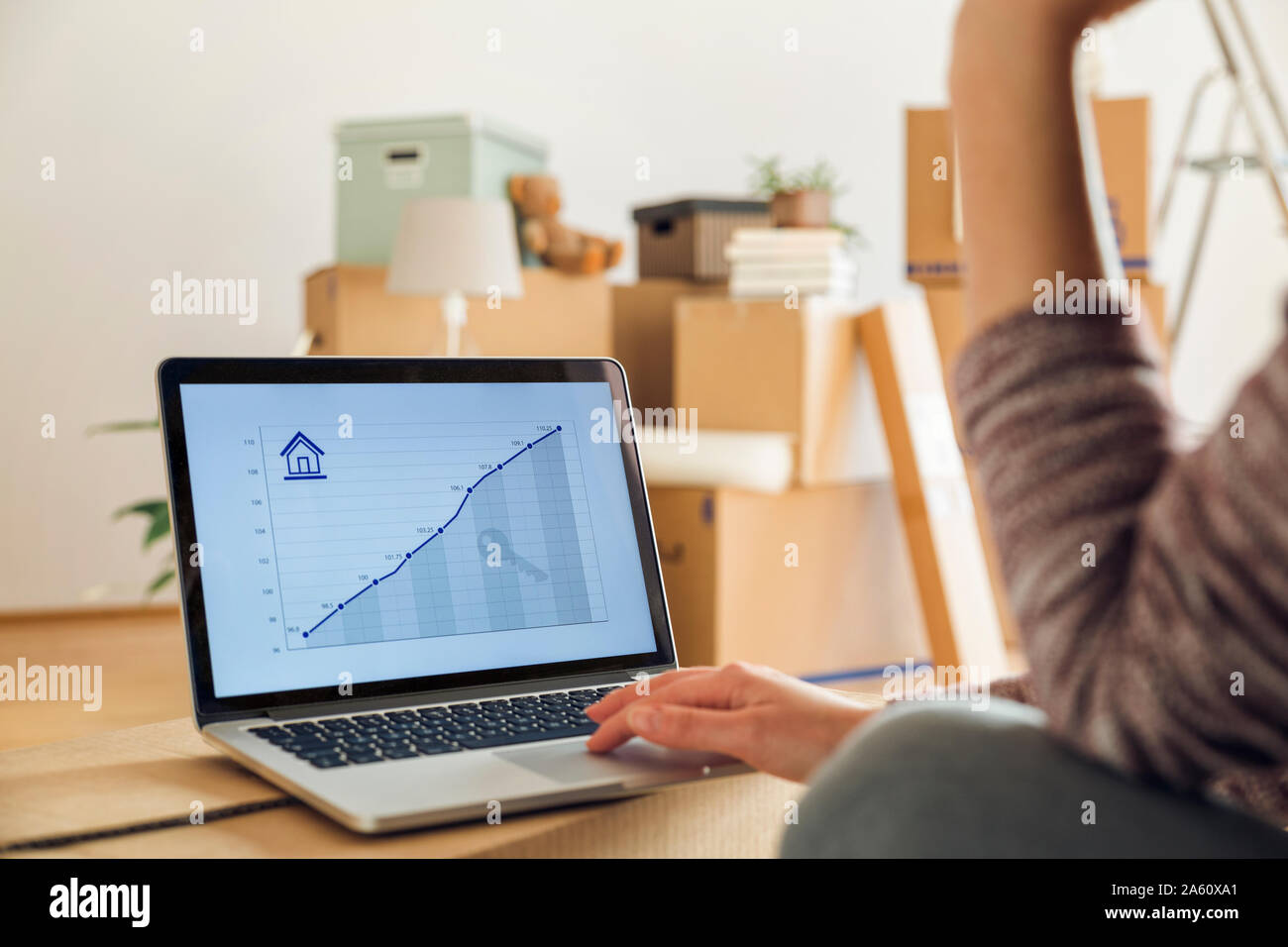 Woman using laptop with rising line graph on the screen in a new home ...