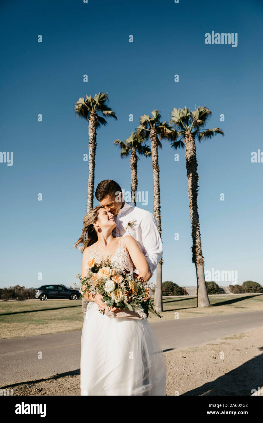 Happy bride and groom hugging at palm trees under blue sky Stock Photo ...