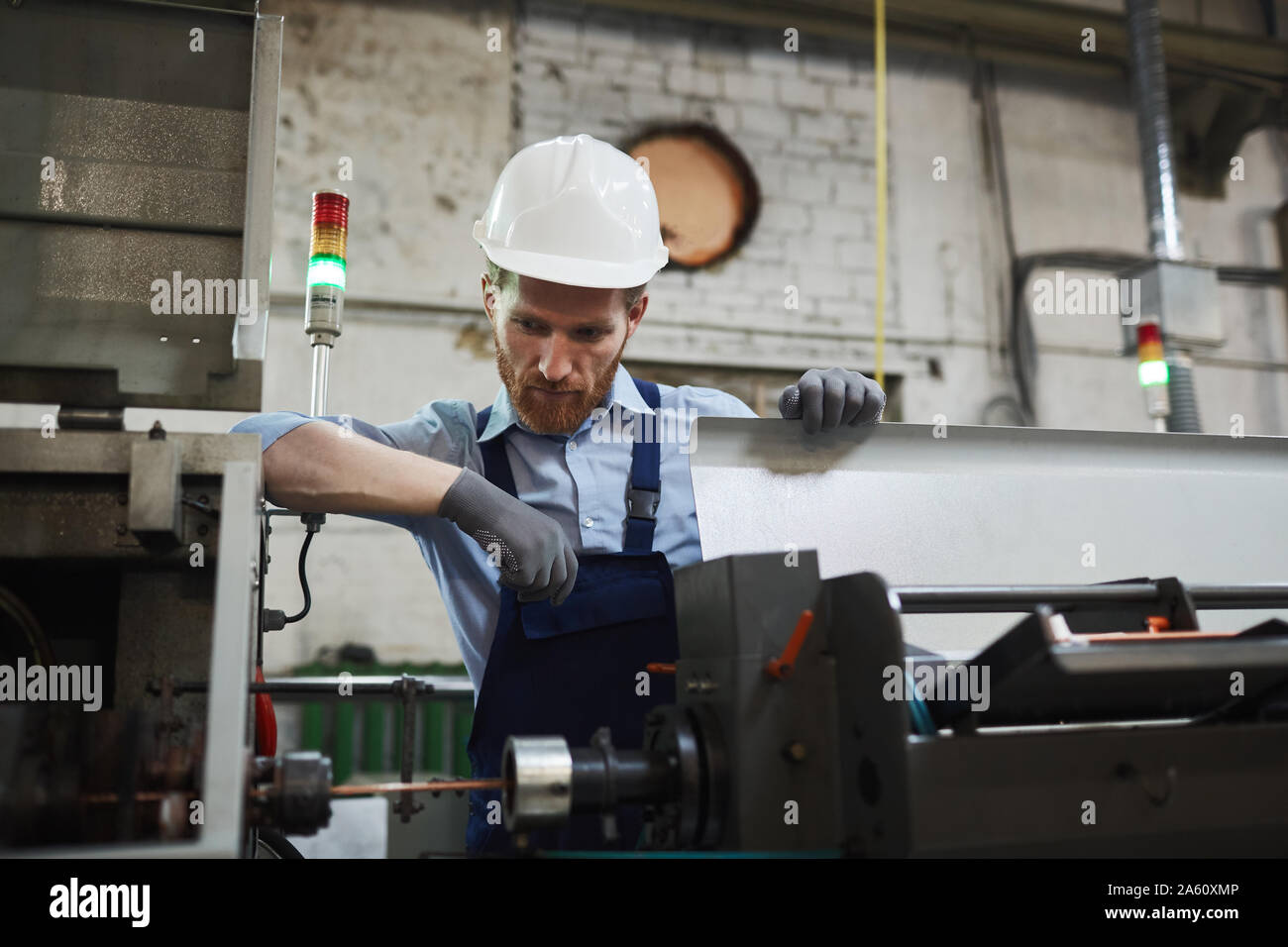 Young engineer in overalls and in work helmet standing and examining ...