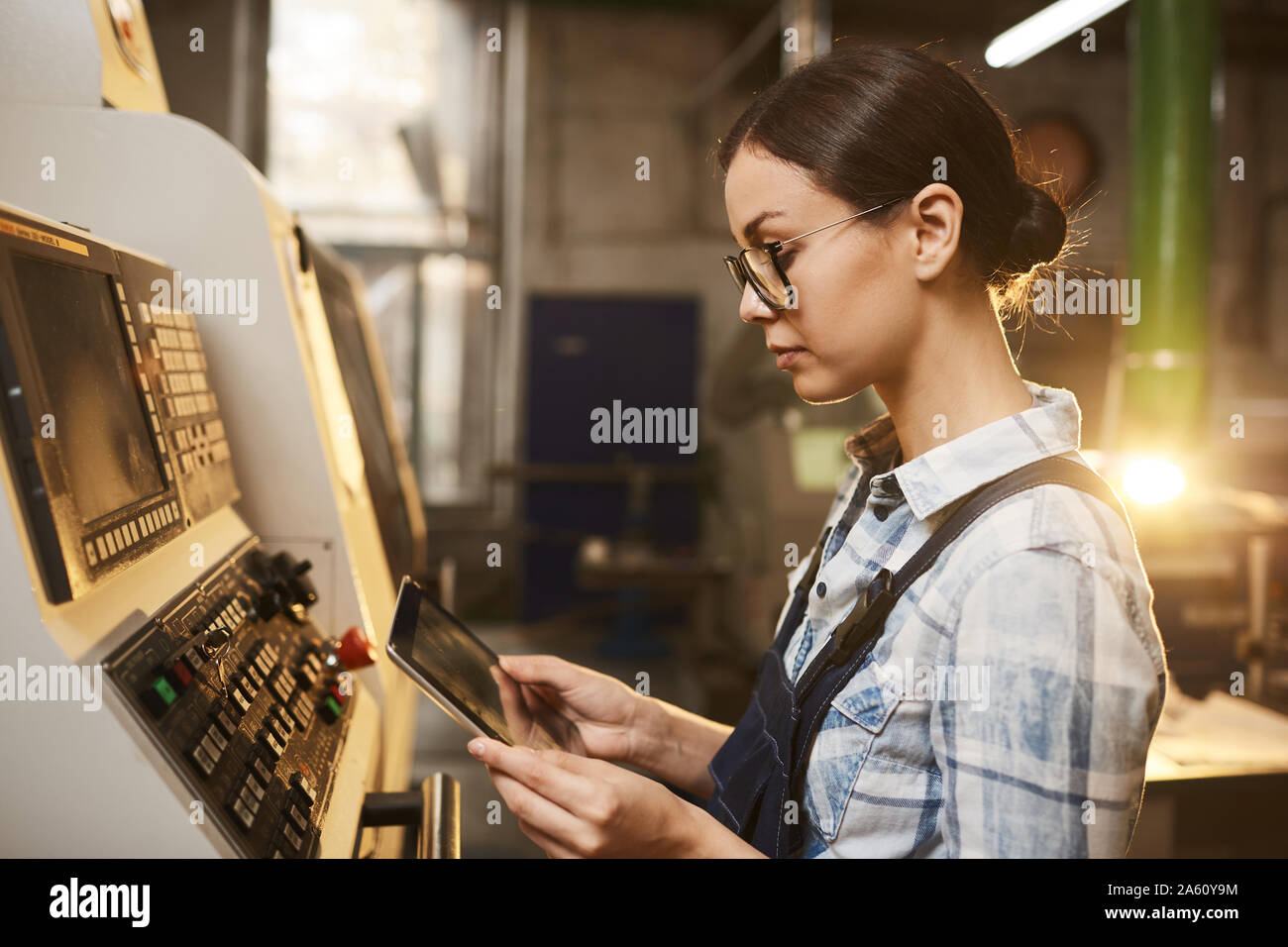 Female operator in eyeglasses standing near the machine and controlling ...