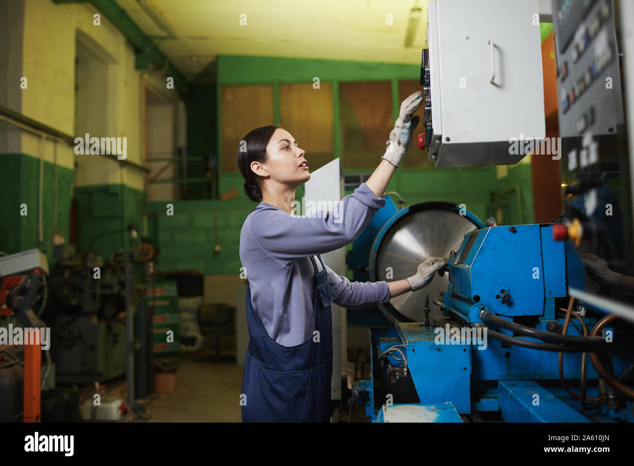 Young female worker in overalls standing and pushing buttons on the ...