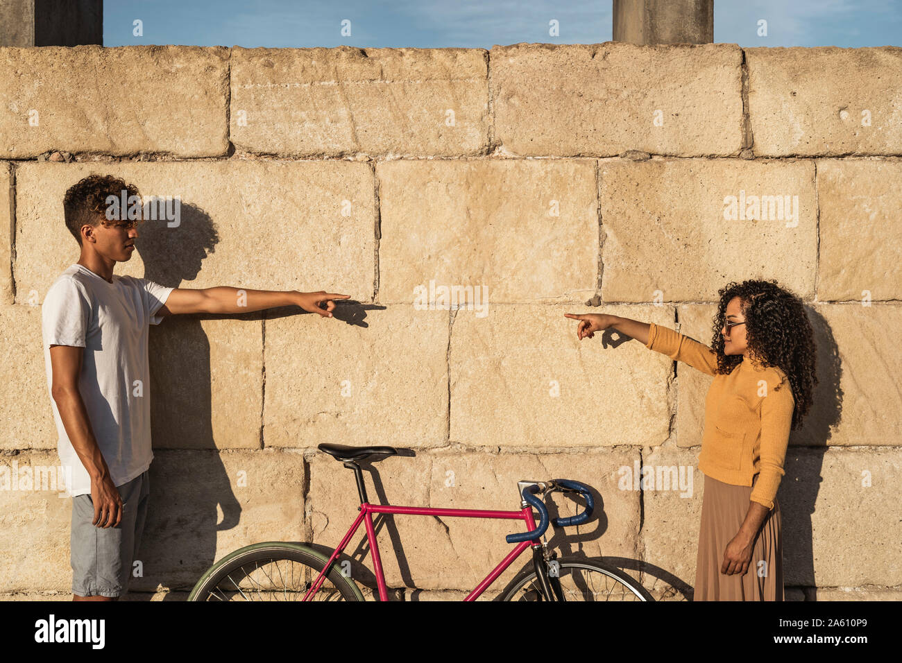 Young couple standing in front of wall, pointing at eachother Stock ...