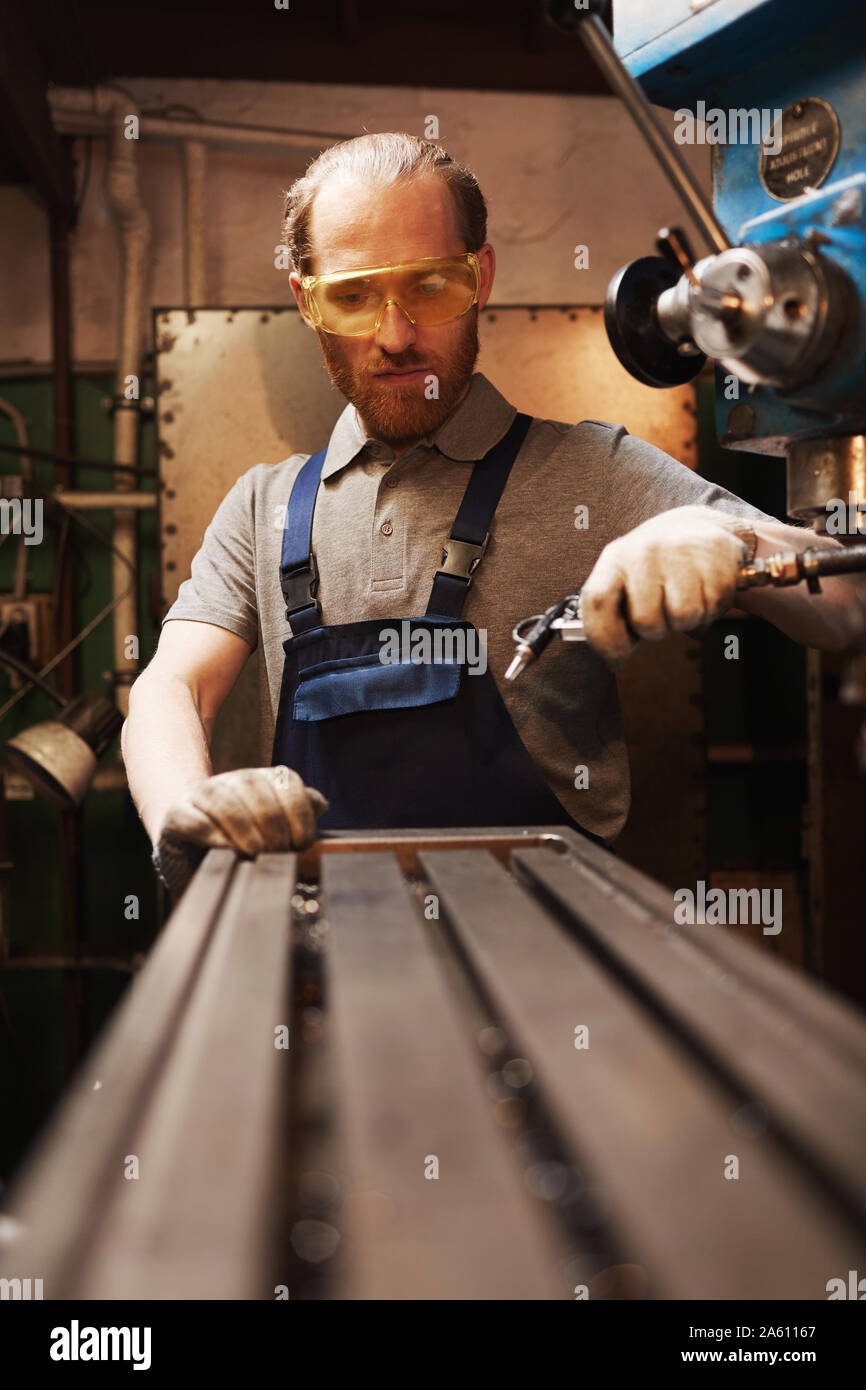 Bearded young manual worker in protective glasses working with metal on ...