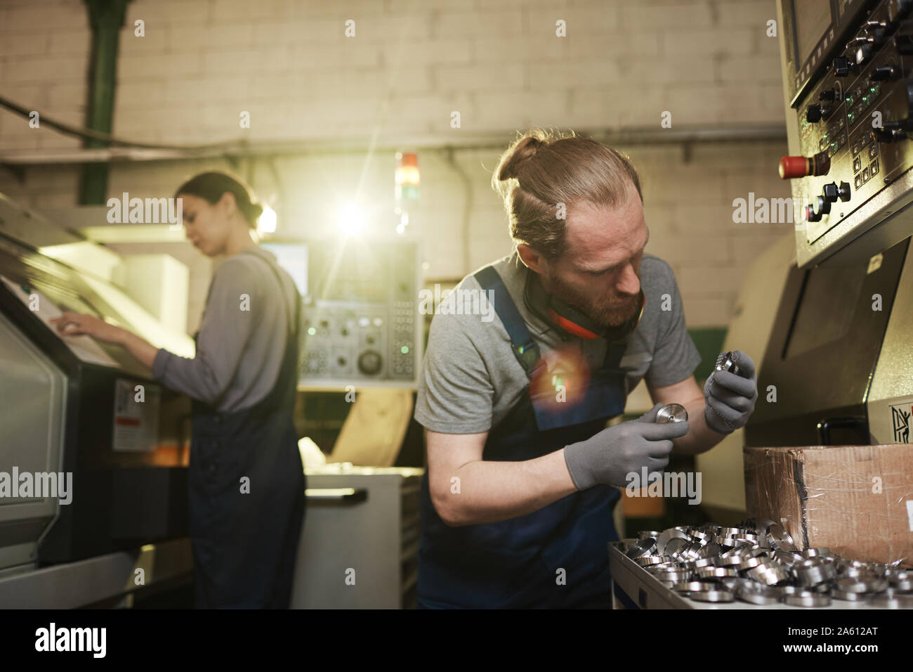 Young mechanic in work wear examining metal details and working on ...
