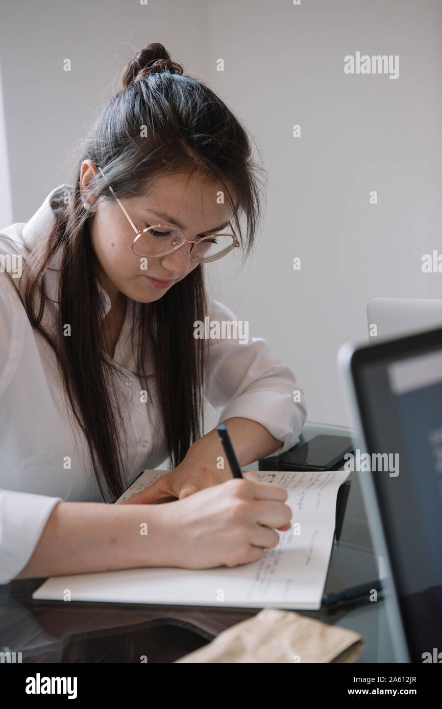 Young woman working at table in office taking notes Stock Photo - Alamy