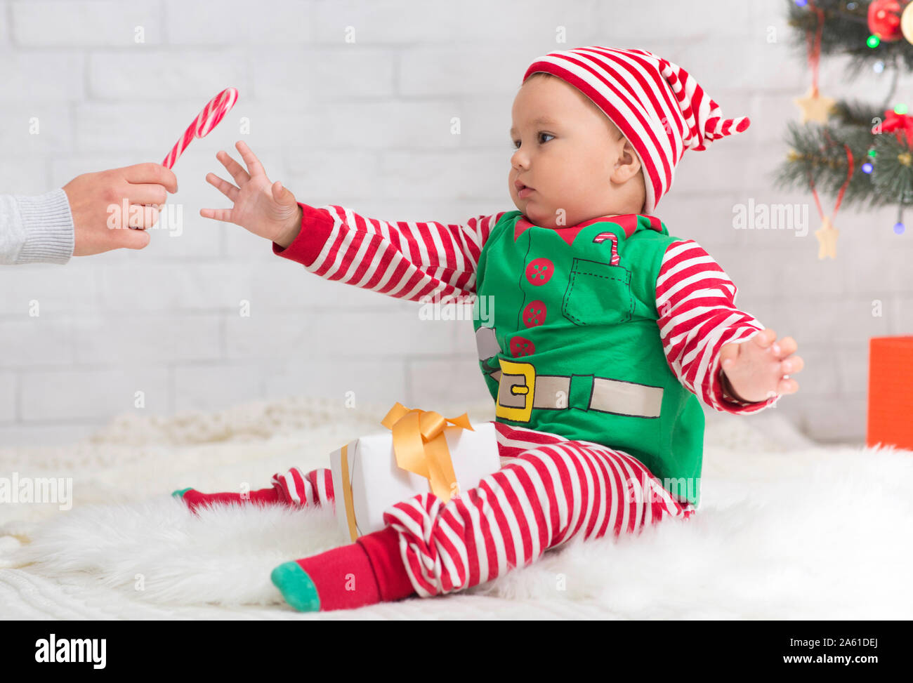 Cute baby elf reaching hand for Christmas lollipop Stock Photo - Alamy