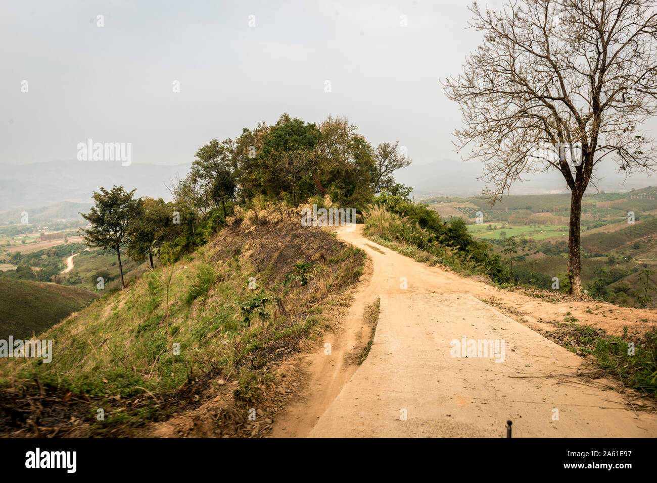 A winding dirt path leads through serene hills towards a remote hill ...