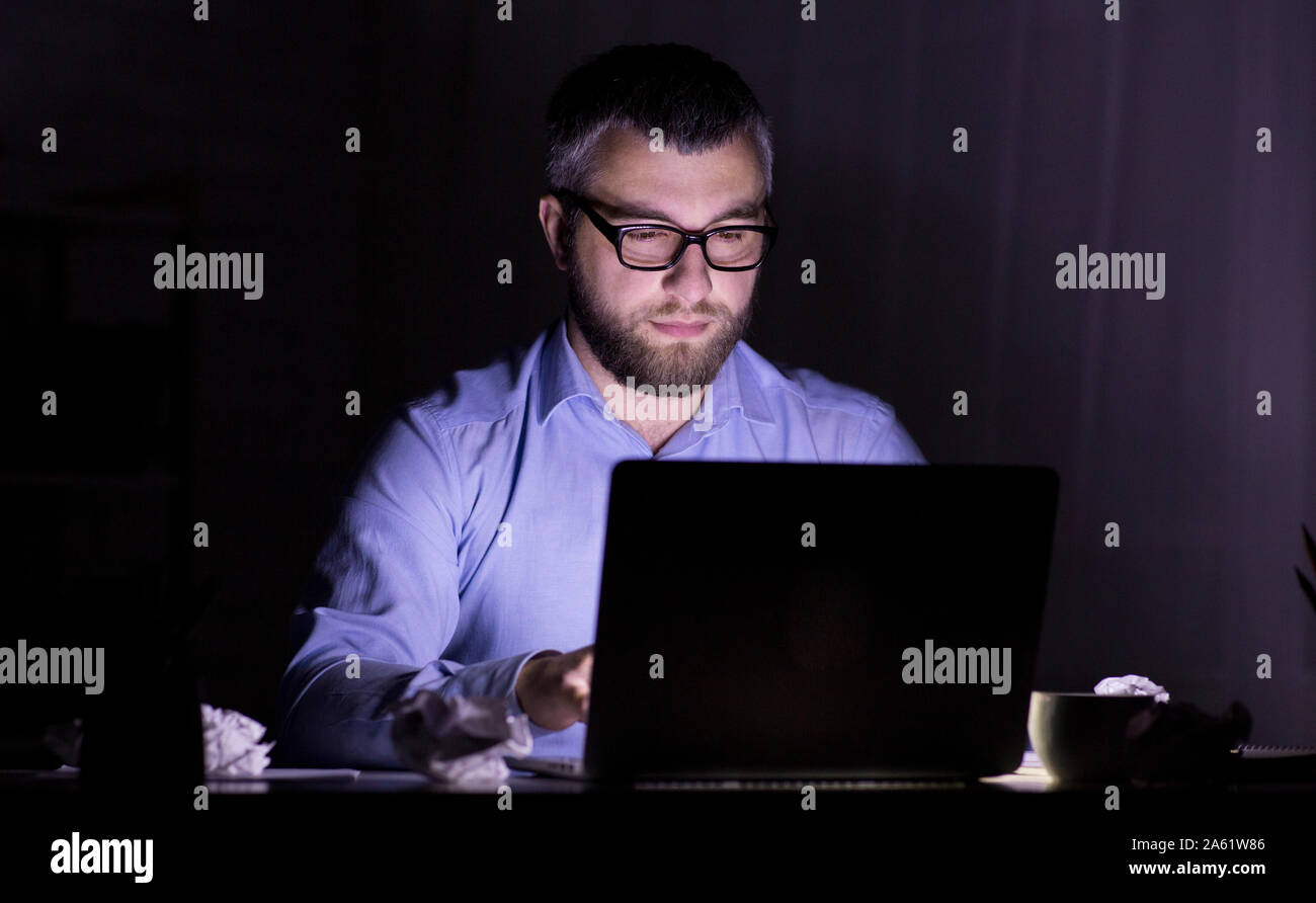 Puzzled man looking at laptop screen in dark room Stock Photo - Alamy