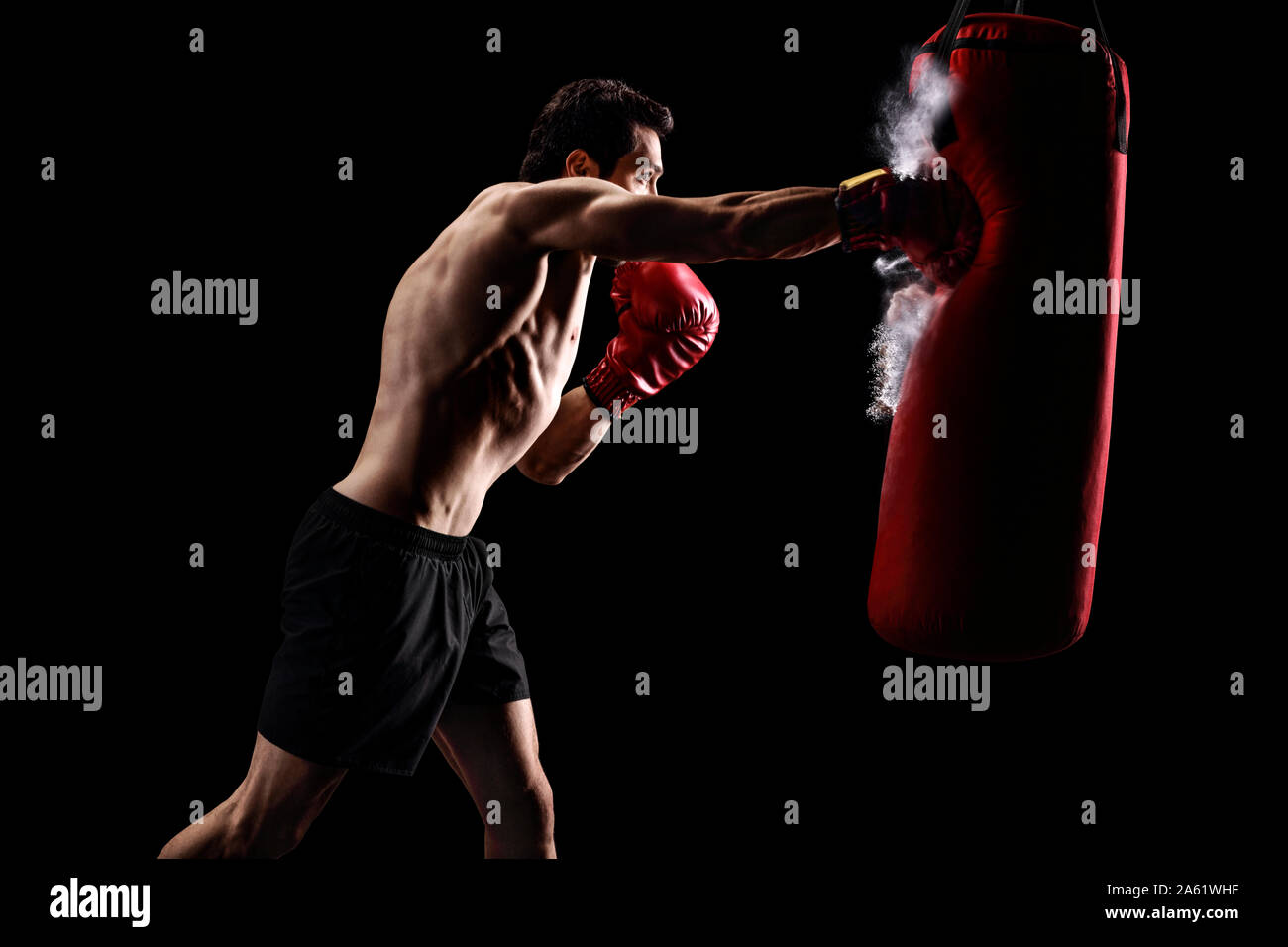 Strong muscular man punching a bag with boxing gloves on a black ...