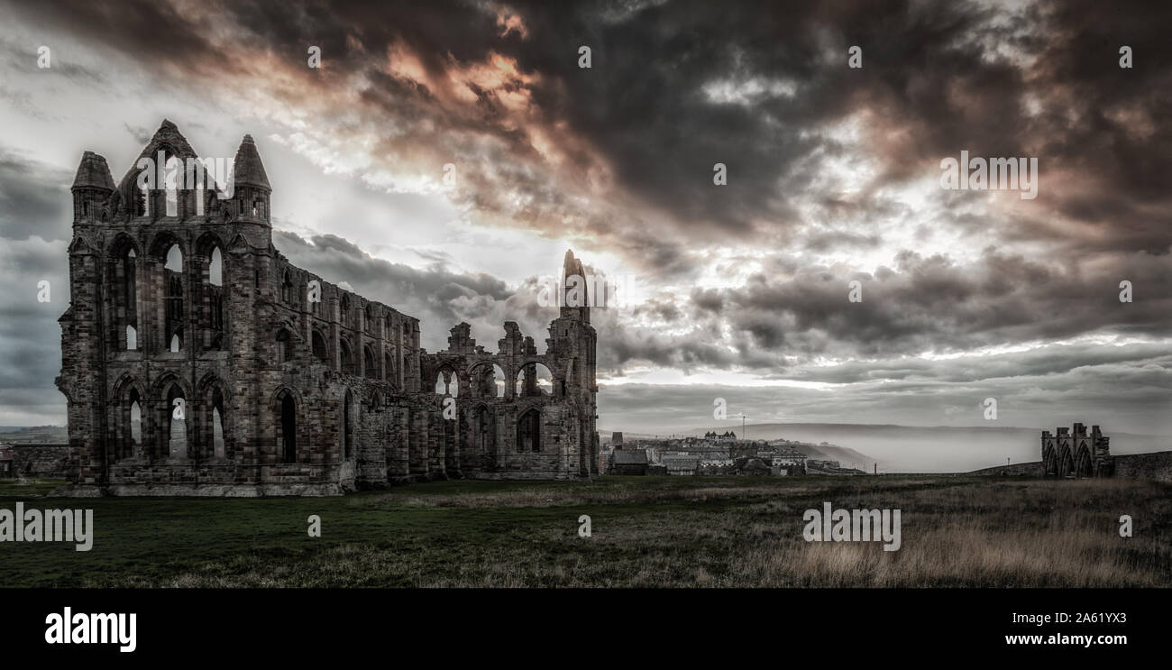 A spooky Whitby Abbey at sunset with a moody sky and the town in the ...