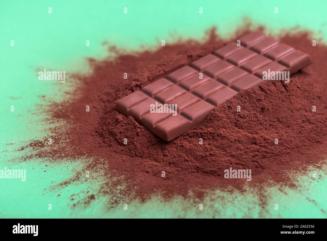 Close-up of chocolate bar and cocoa powder pile on green background ...