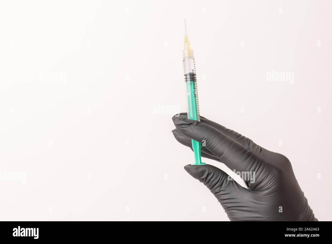 Hand in black glove with a filled syringe with a needle on a white ...