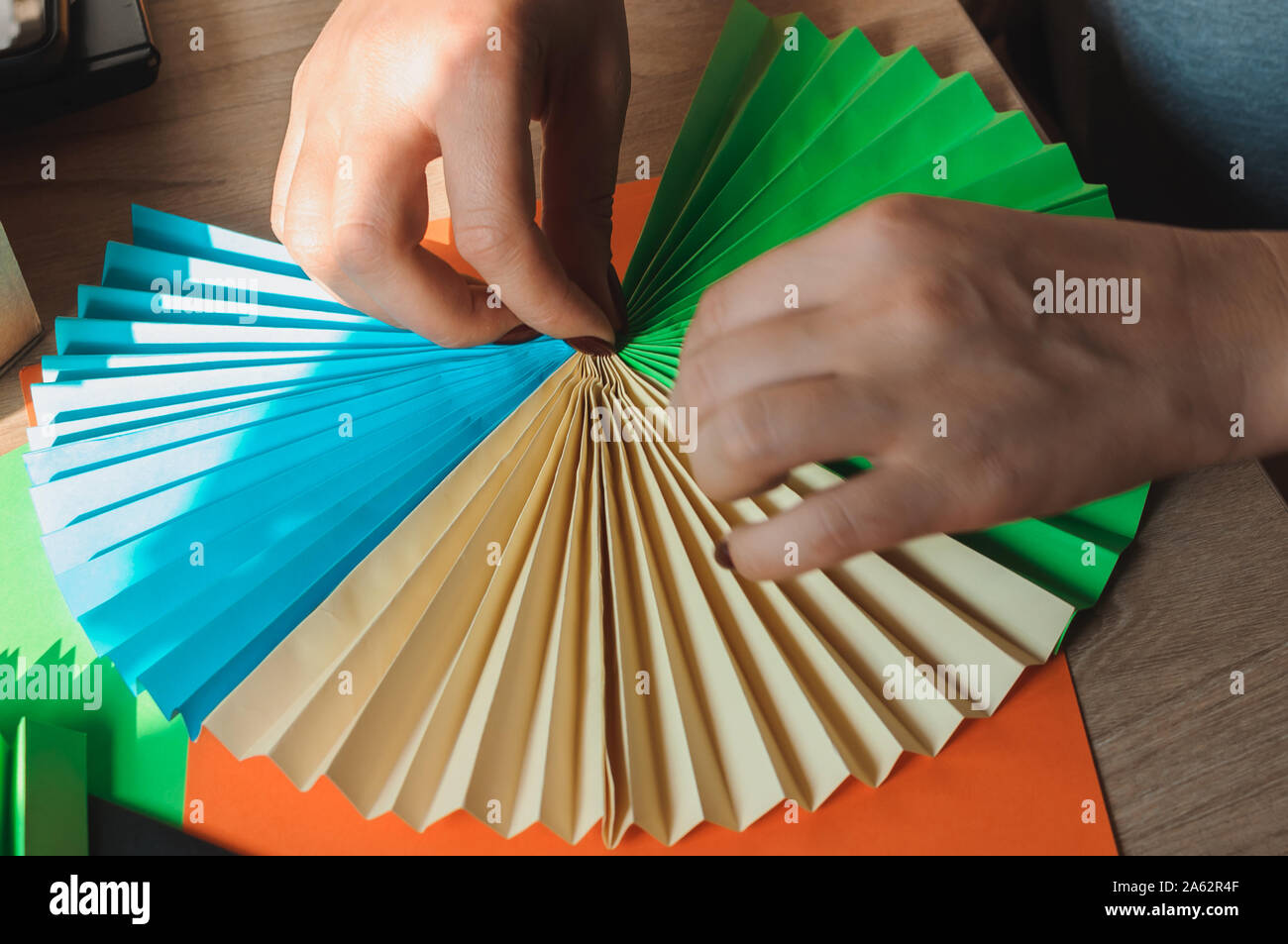 In the foreground female hands glue origami fans, sheets of colored ...