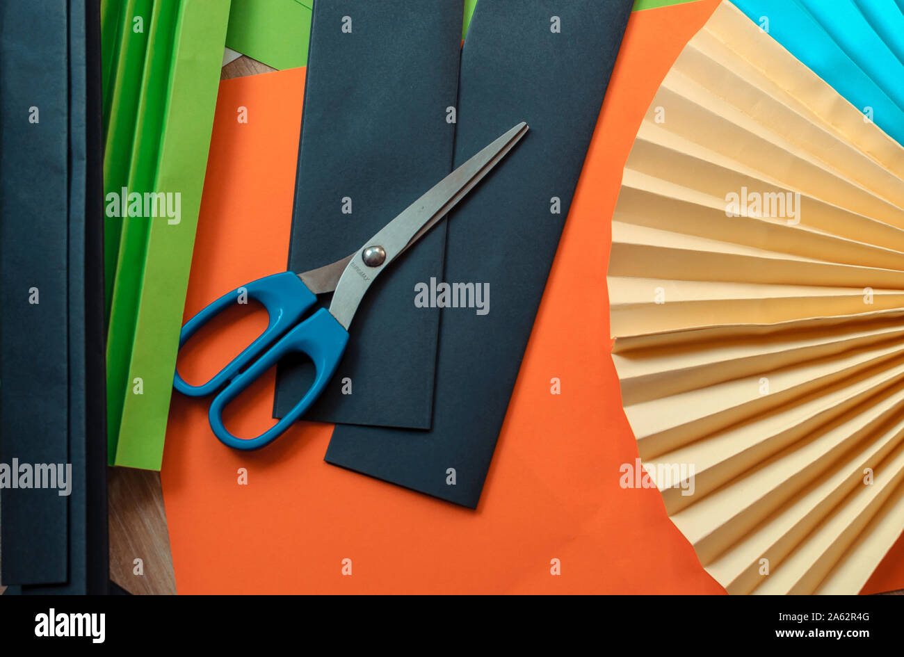 Origami colorful fans, sheets of paper, scissors on a wooden table ...