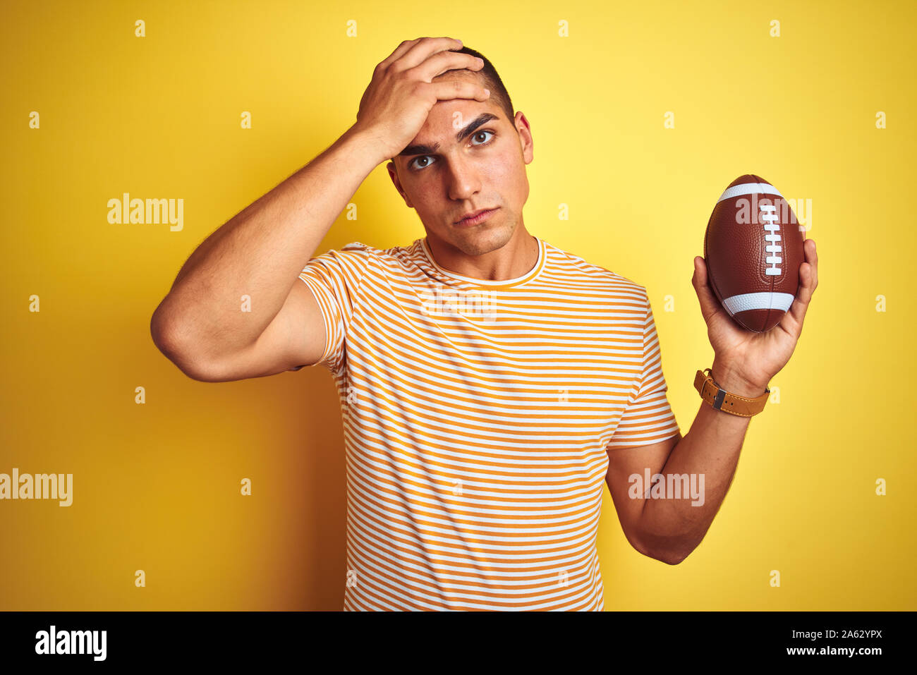 Young rugby player man holding a football ball over yellow isolated ...