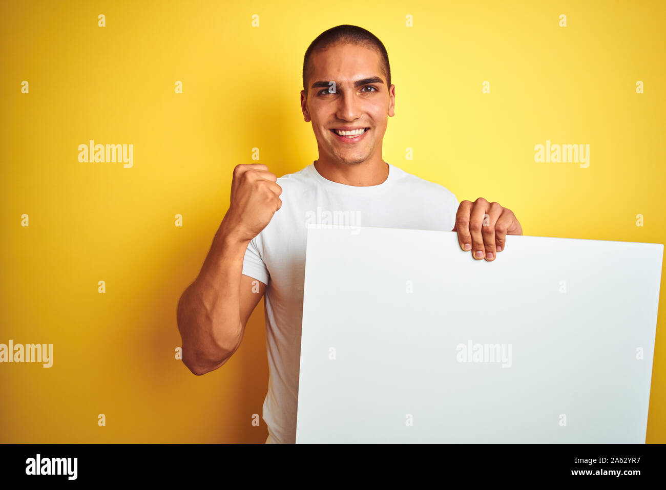 Young handsome man holding advertising banner over yellow isolated ...