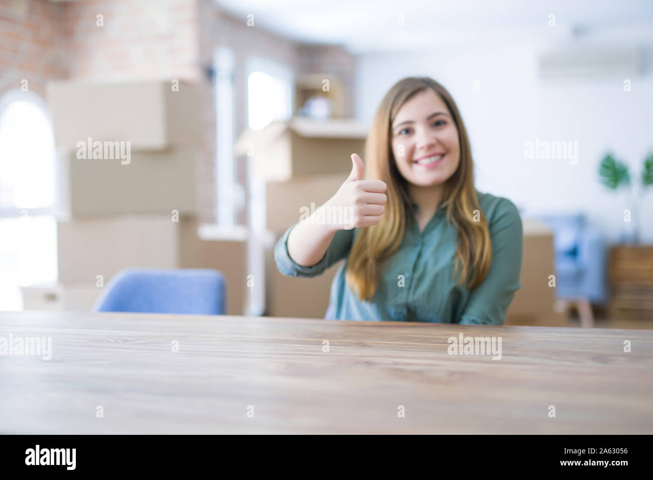 Young woman sitting on the table with cardboard boxes behind her moving ...