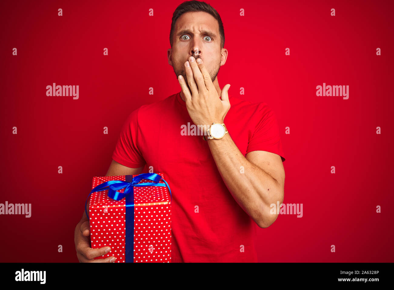 Young man holding birthday present over isolated red background cover ...