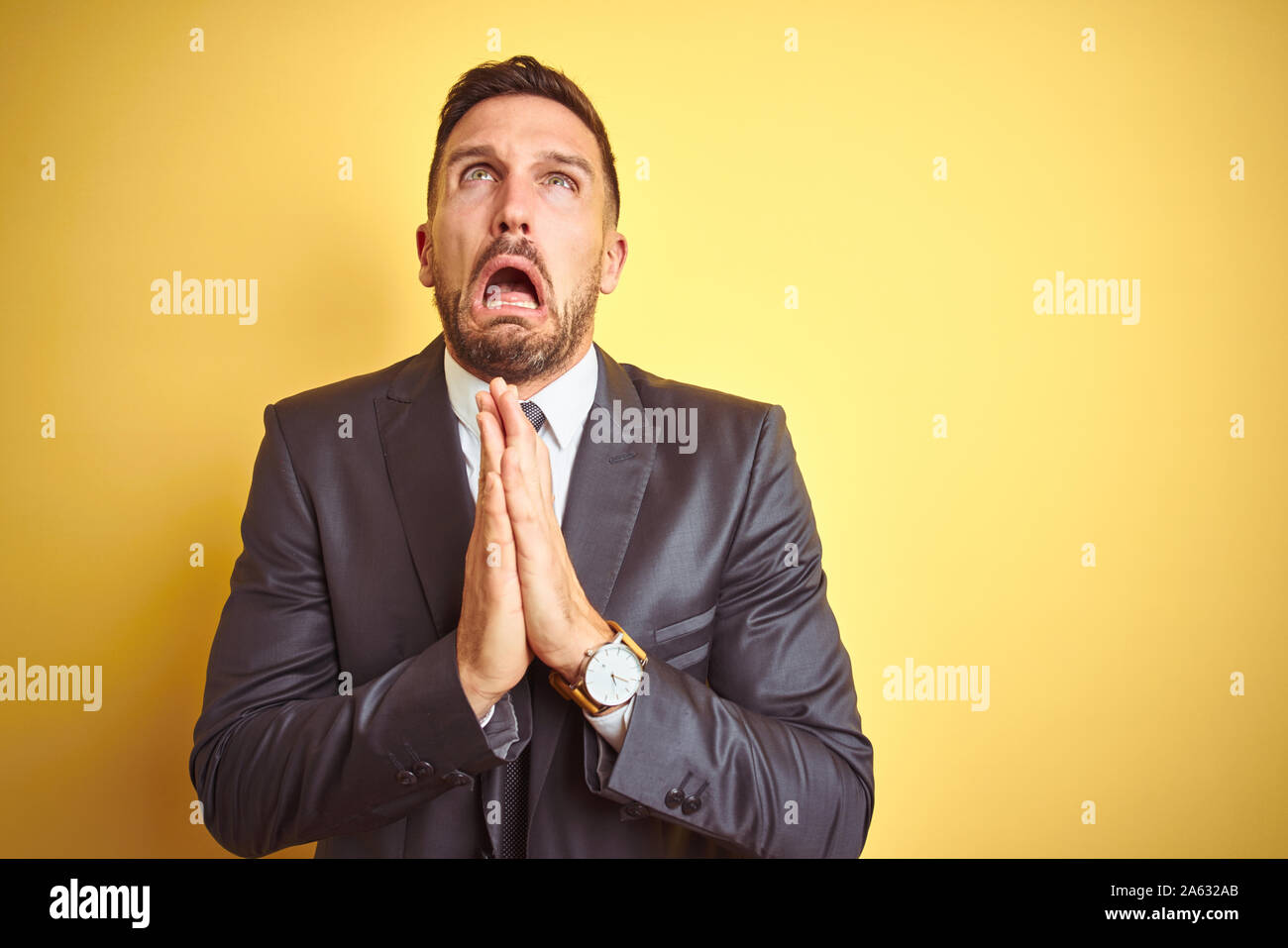 Young handsome business man over yellow isolated background begging and ...