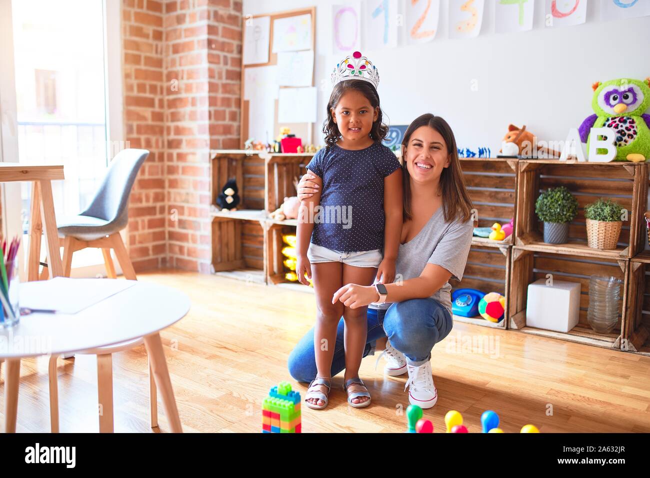 Beautiful teacher looking at toddler girl wearing princess crown at ...