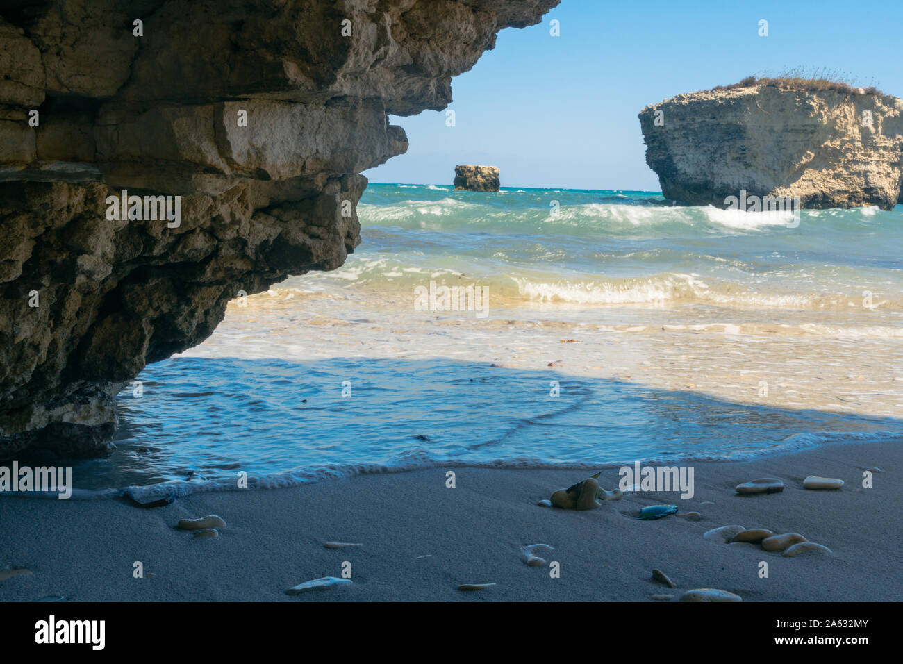 under a shady cliff the sea meets a tiny beach during the summer day ...