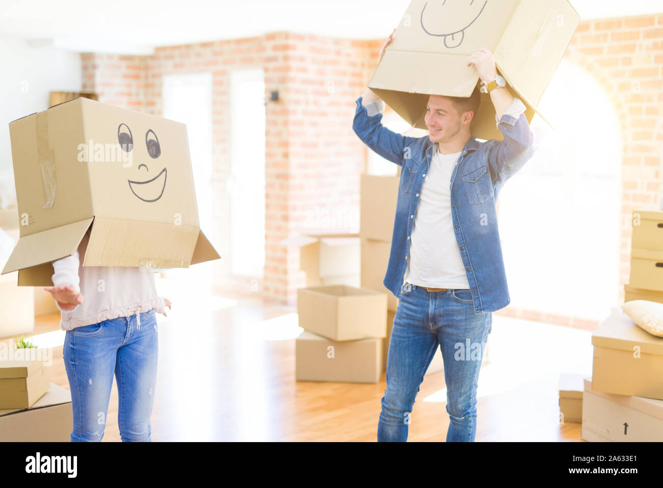 Couple having fun at new apartment wearing boxes with funny faces over ...