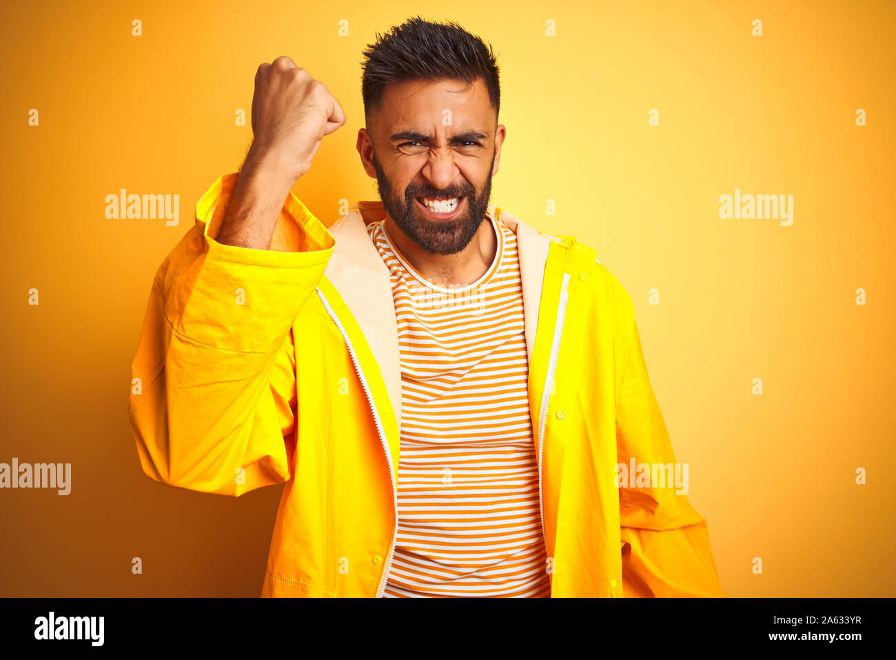 Young indian man wearing raincoat standing over isolated yellow ...