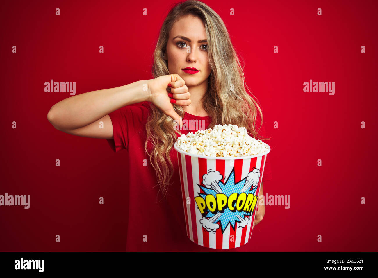 Young beautiful woman wearing t-shirt eating popcorn over red isolated ...