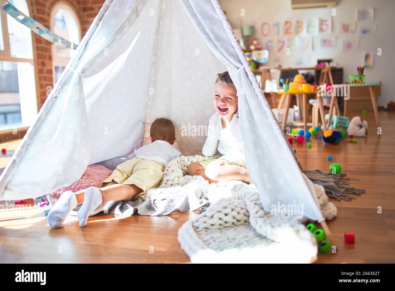 Adorable blonde twins playing inside tipi around lots of toys at ...