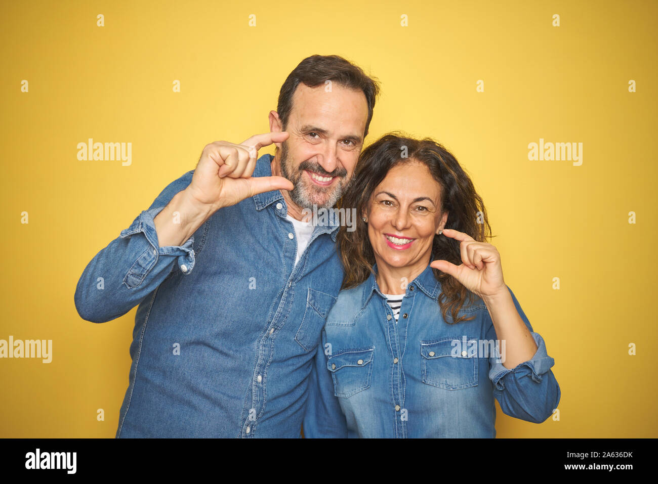 Beautiful middle age couple together standing over isolated yellow ...