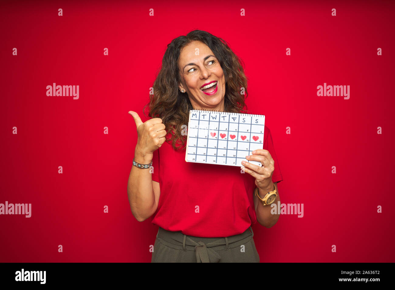 Middle age senior woman holding menstruation calendar over red isolated ...