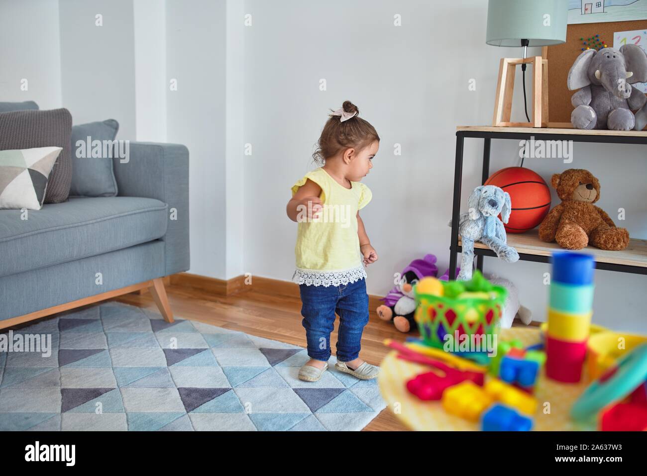 Beautiful toddler standing looking at shelving with dolls at ...