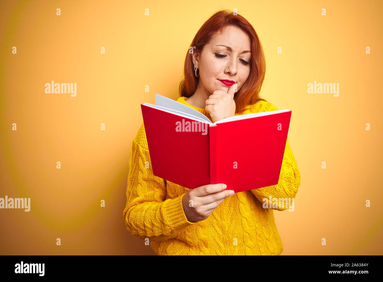 Young redhead teacher woman reading red book over yellow isolated ...