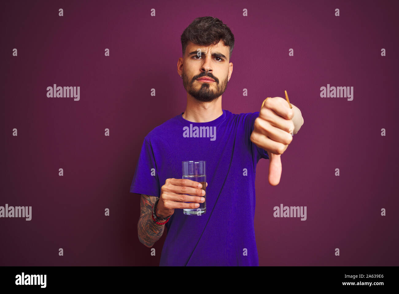Young man with tattoo drinking glass of water standing over isolated ...