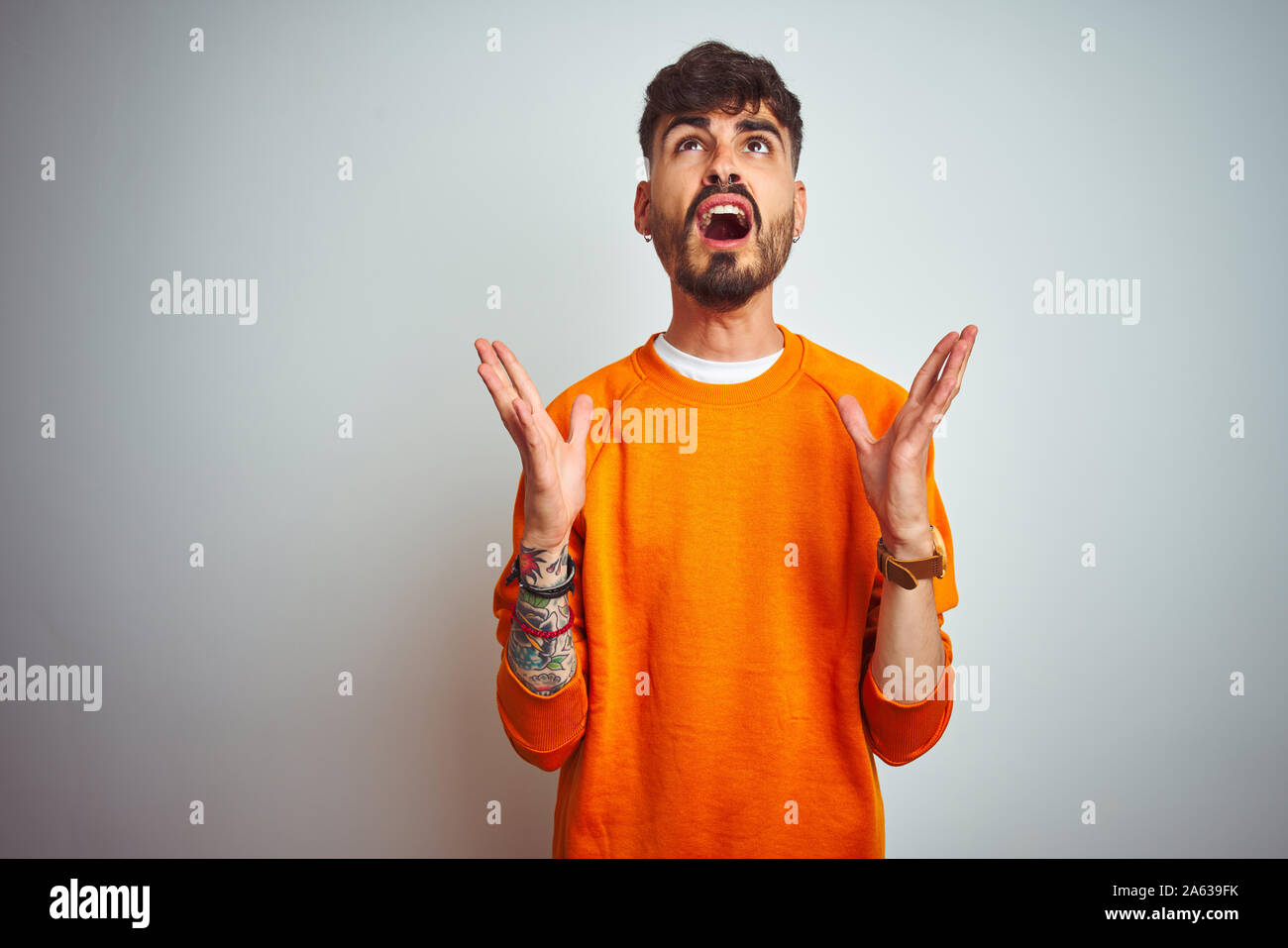 Young man with tattoo wearing orange sweater standing over isolated ...
