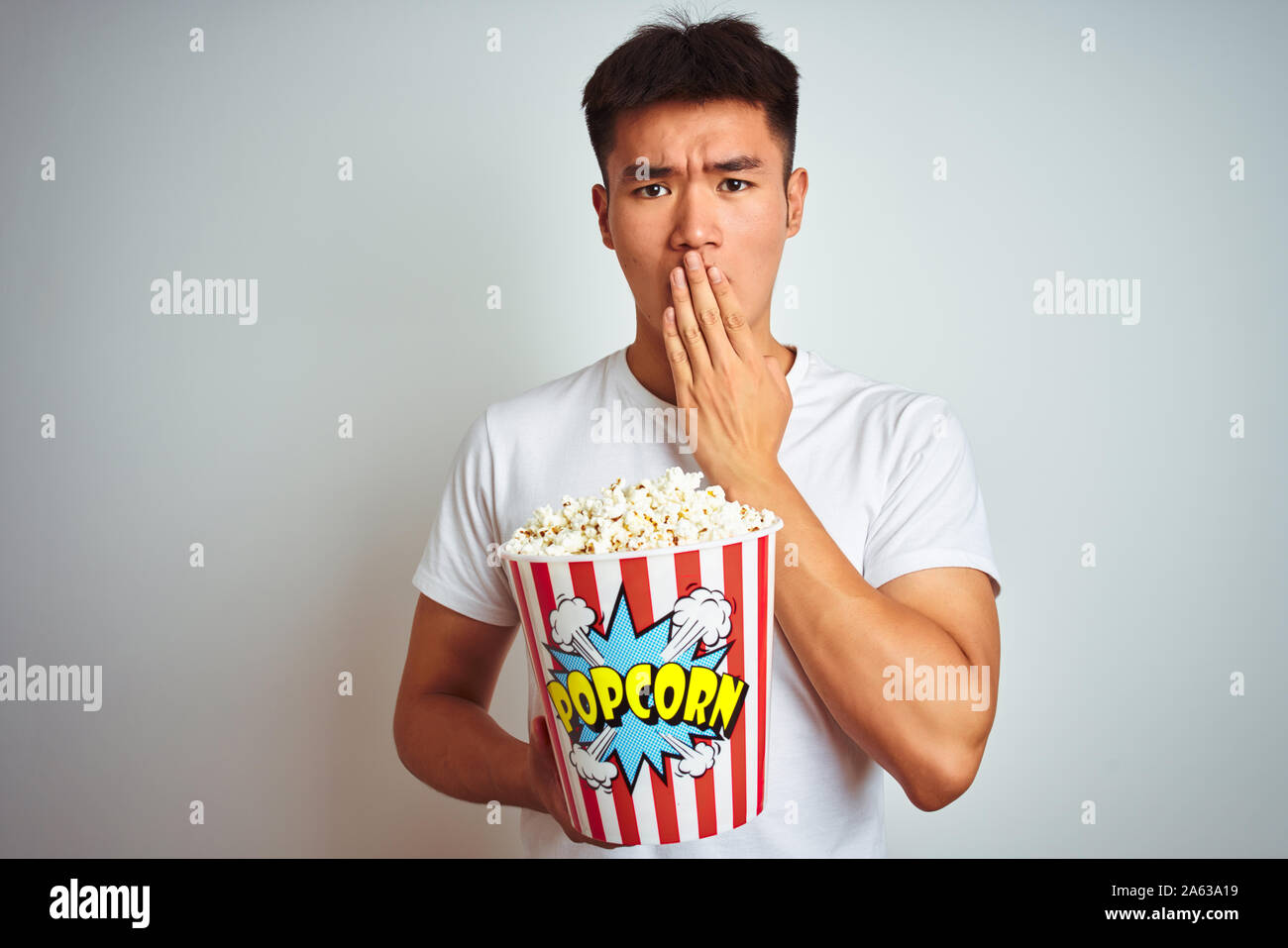 Young asian chinese man holding pack of popcorn standing over isolated ...