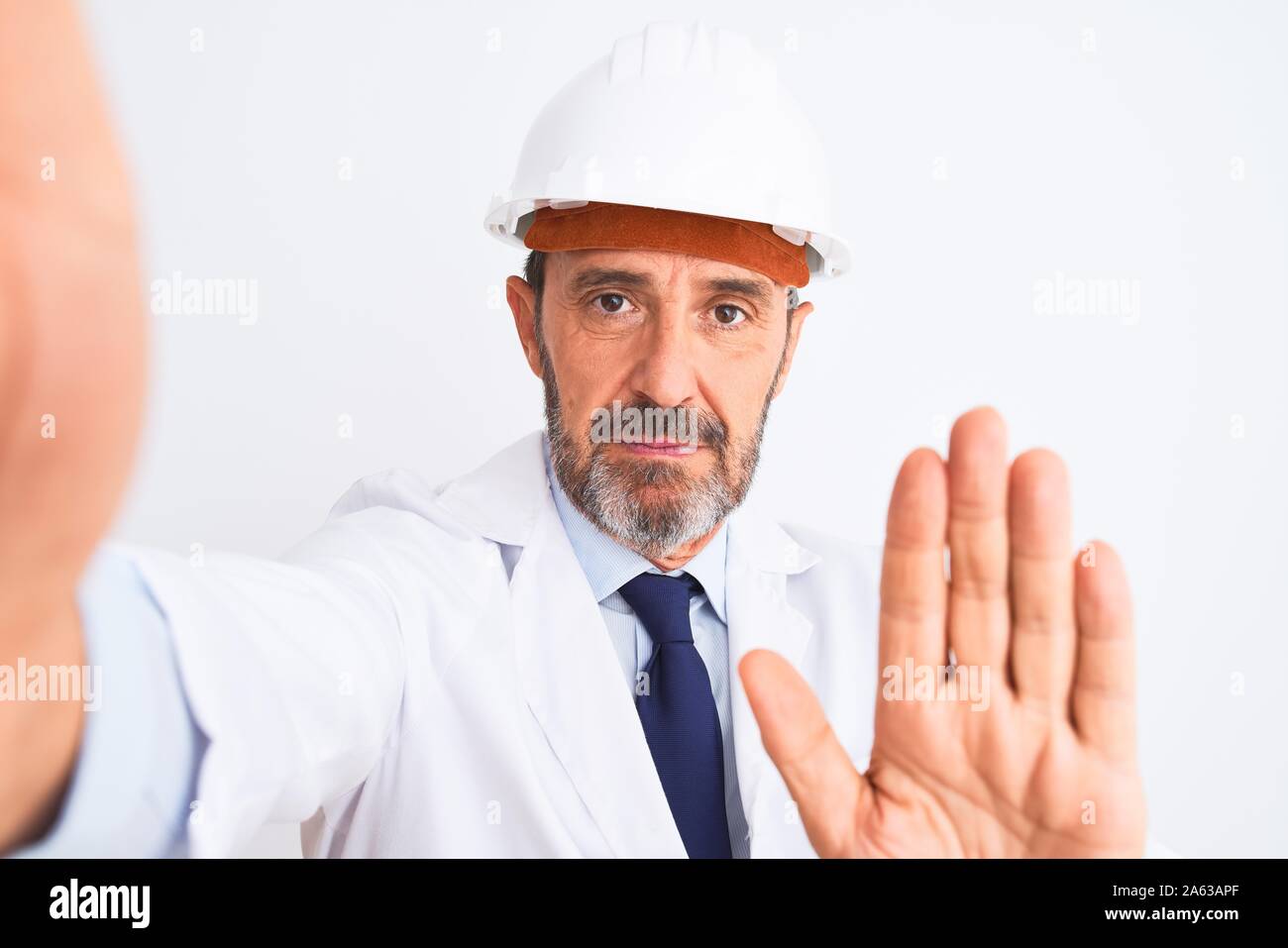 Middle age engineer man wearing helmet make selfie over isolated white ...