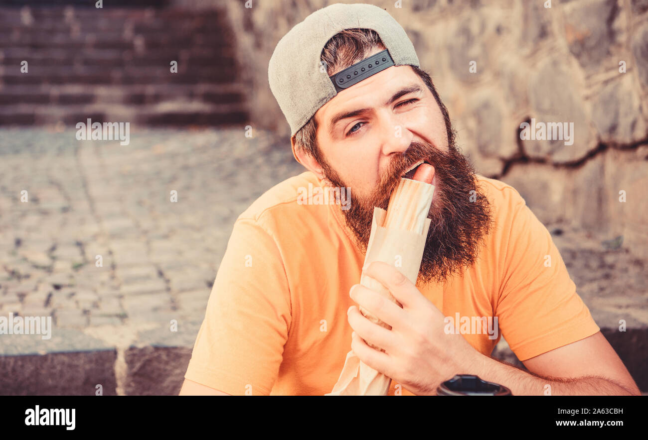 Carefree hipster eat junk food while sit on stairs. Hungry man snack ...