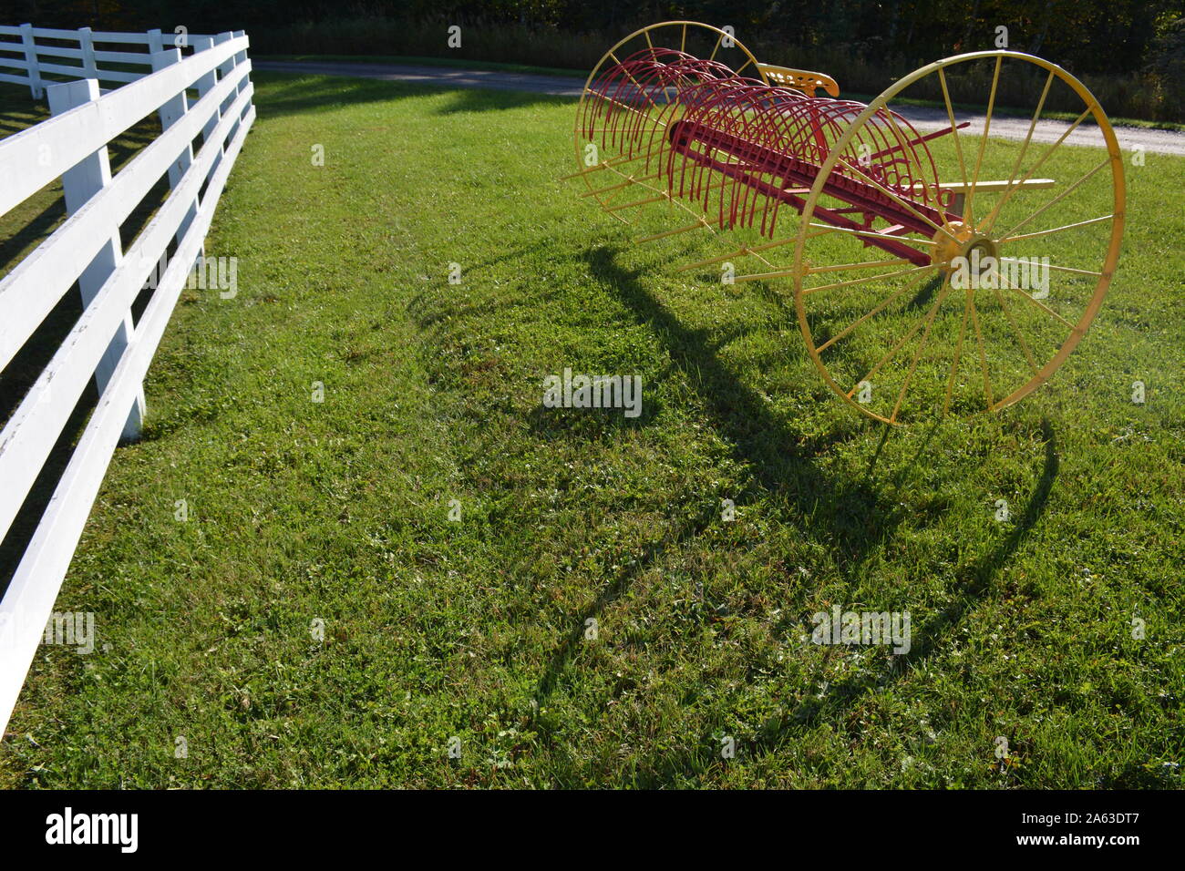 Vintage red and yellow raking machine by white fence Stock Photo - Alamy