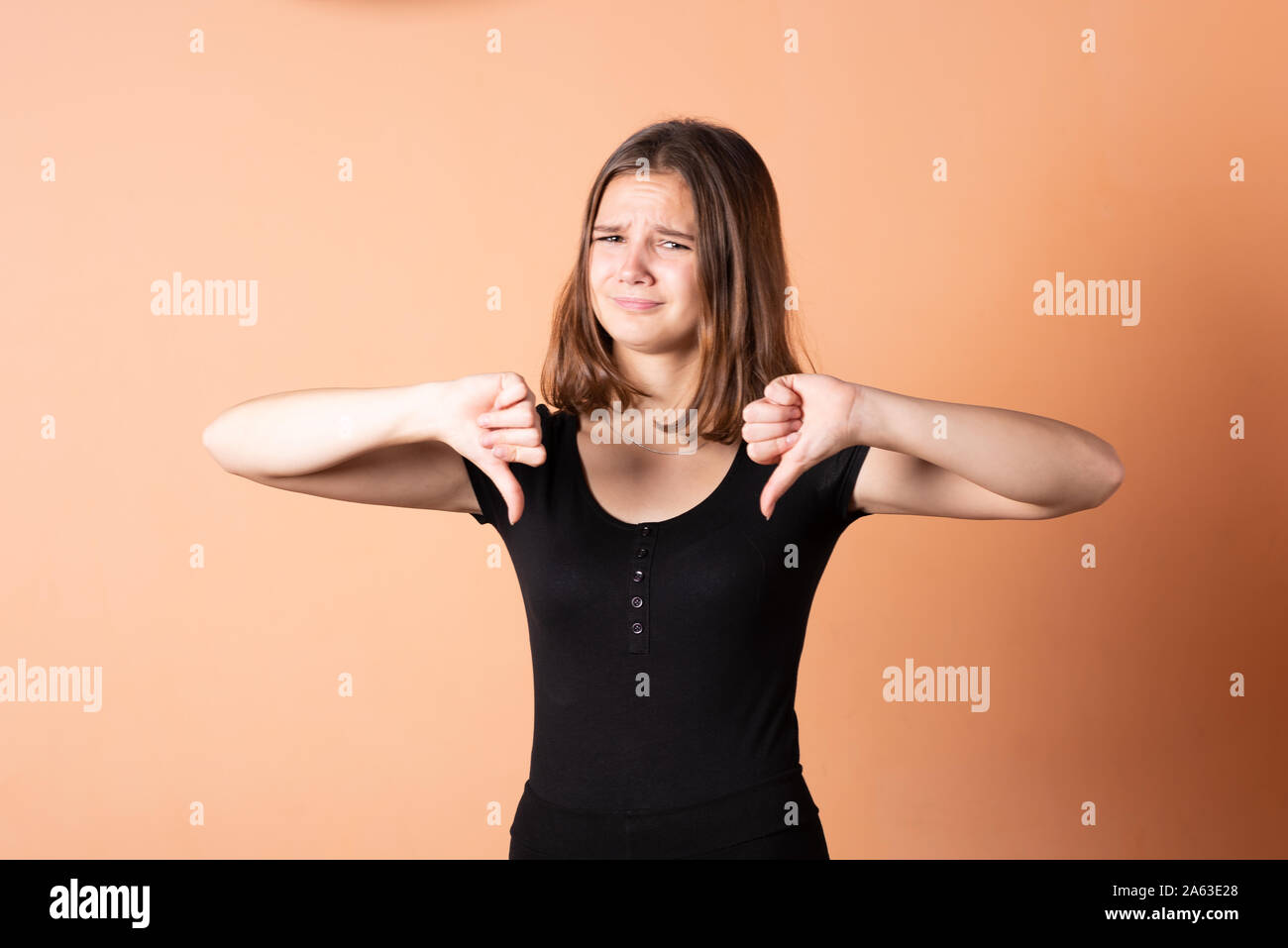 Girl shows a finger down, on a light orange background Stock Photo - Alamy