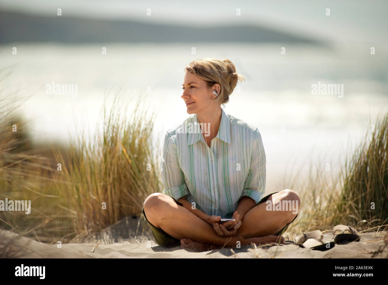 Woman sitting cross legged listening to her music player at the beach ...