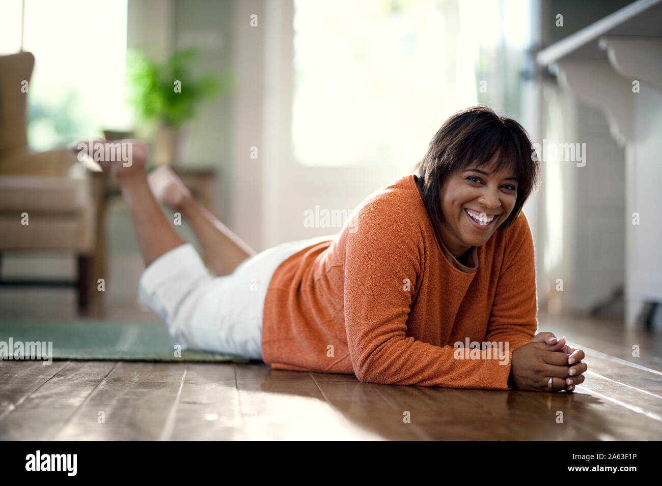 Portrait of a woman lying down relaxing on hardwood living room floor ...