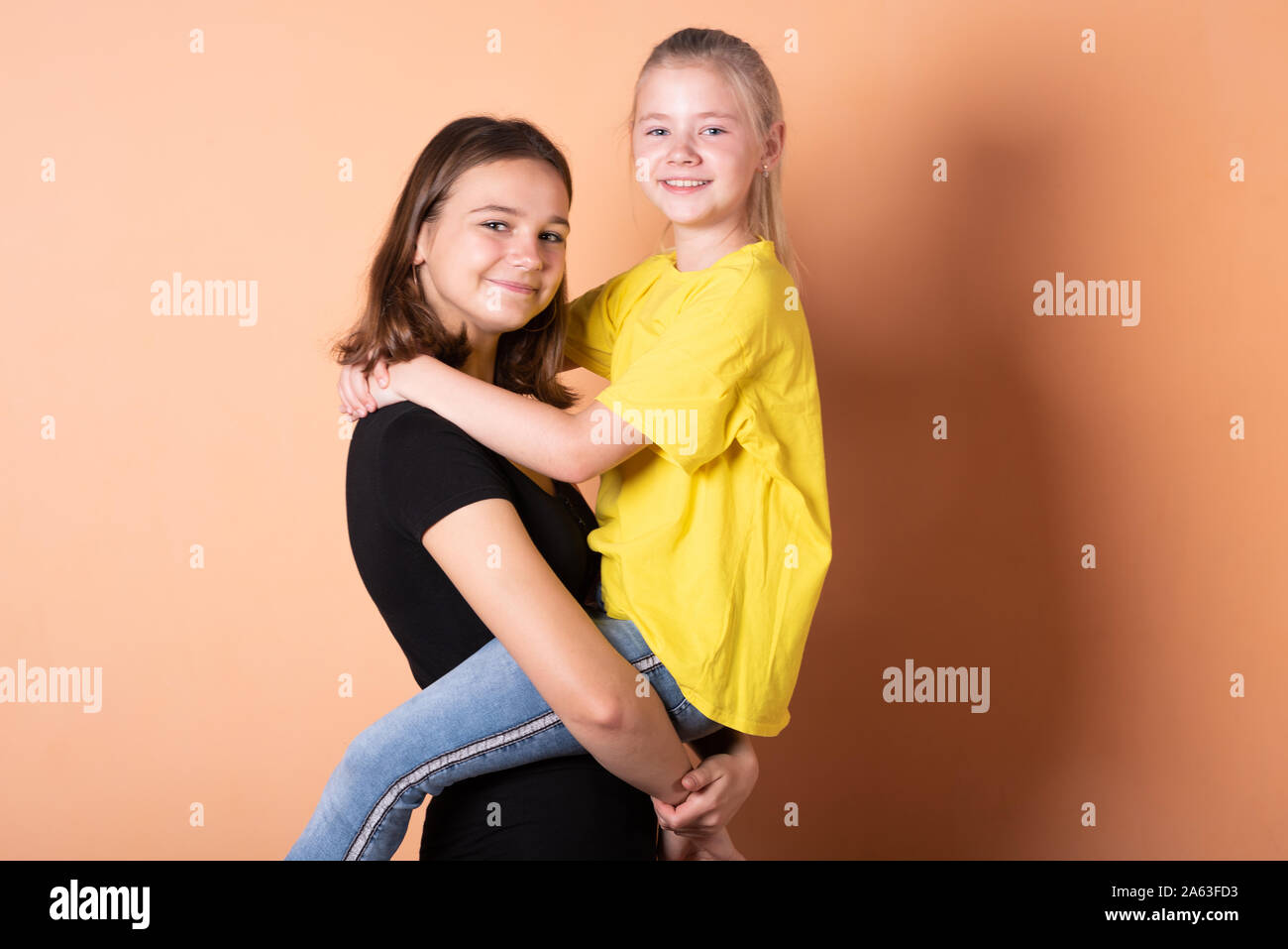 Two girls, sisters, one on the shoulders of the other, on a light ...