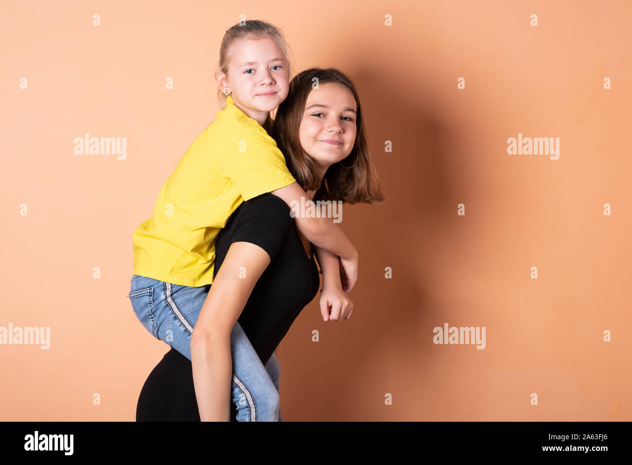 Two girls, sisters, one on the shoulders of the other, on a light ...