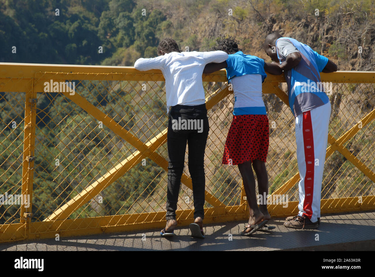 Three people looking over edge of Victoria Falls Bridge, Zimbabwe ...