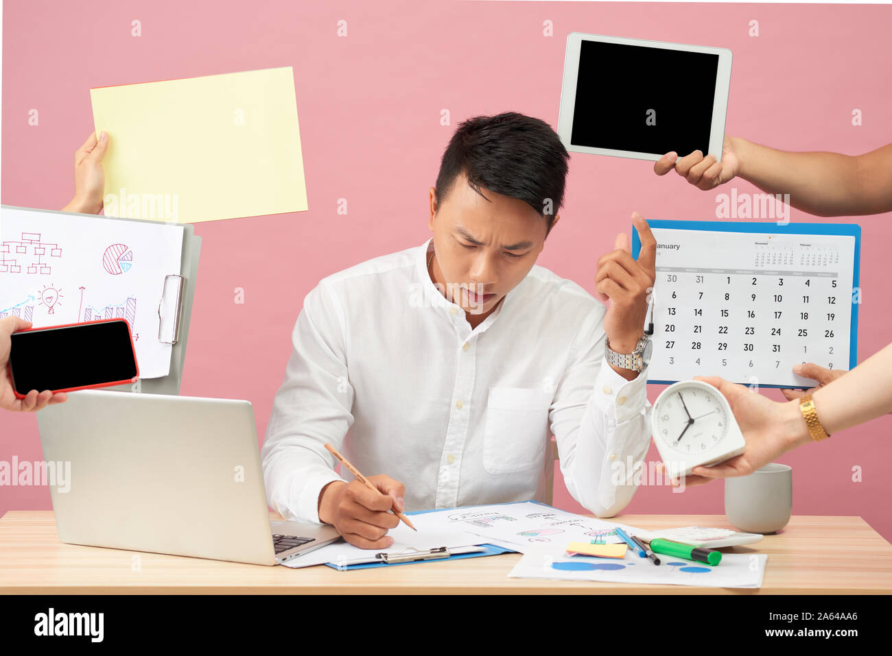 Sad young man sits at desktop, hands with papers, alarm clock, touchpad ...