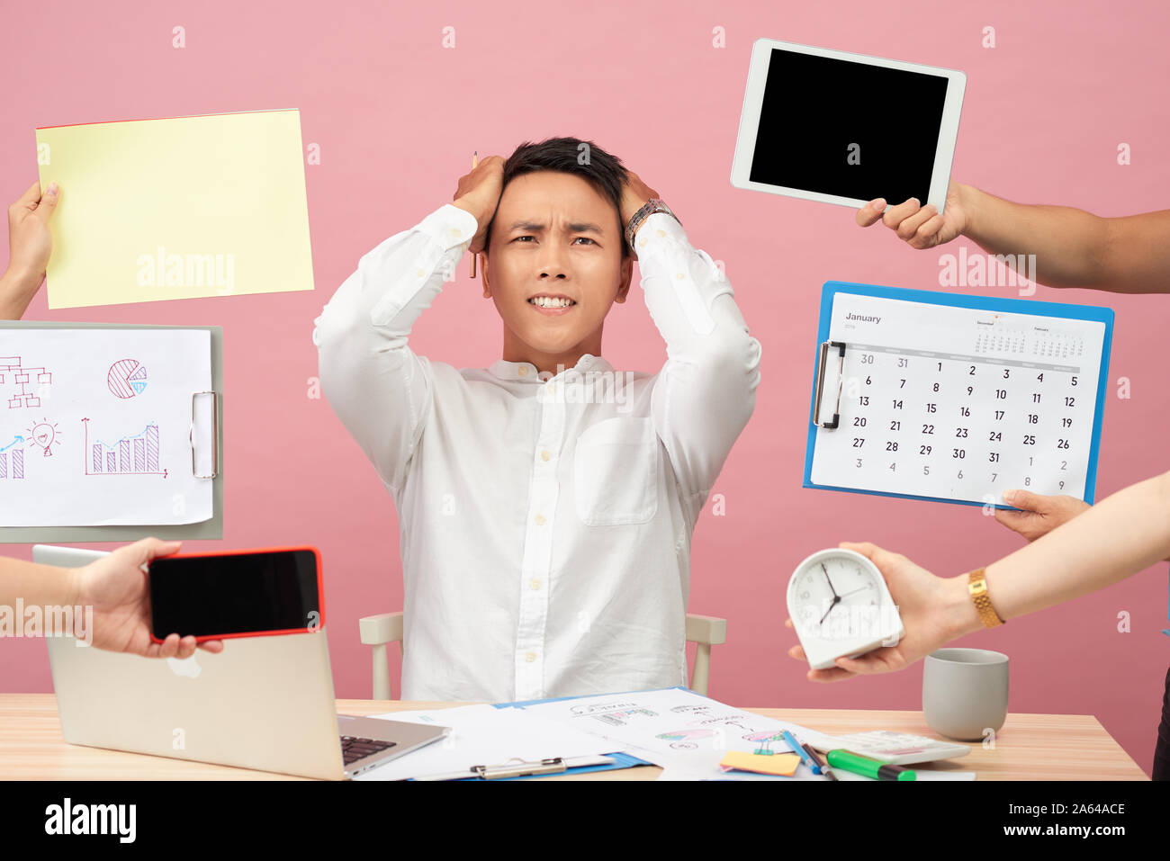 Sad young man sits at desktop, hands with papers, alarm clock, touchpad ...