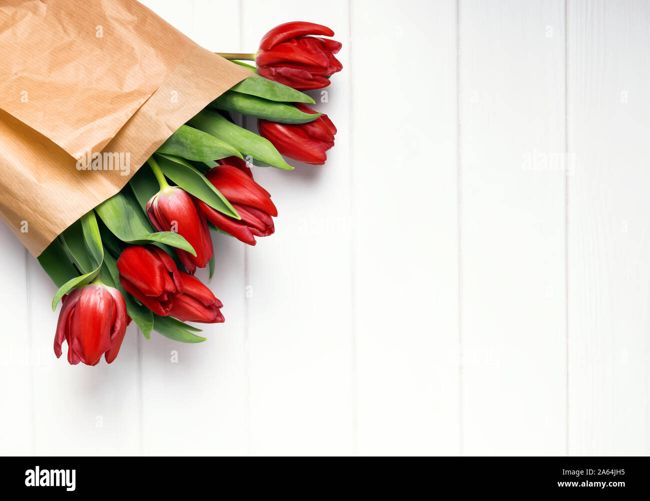 Red tulips wrapped in craft paper on the white wooden table with copy ...