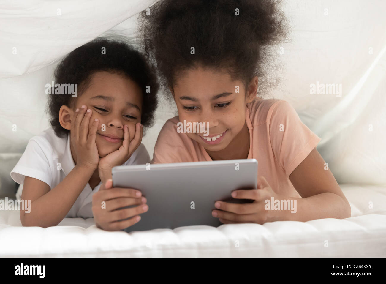 Smiling black siblings watching video on tablet in bed Stock Photo - Alamy