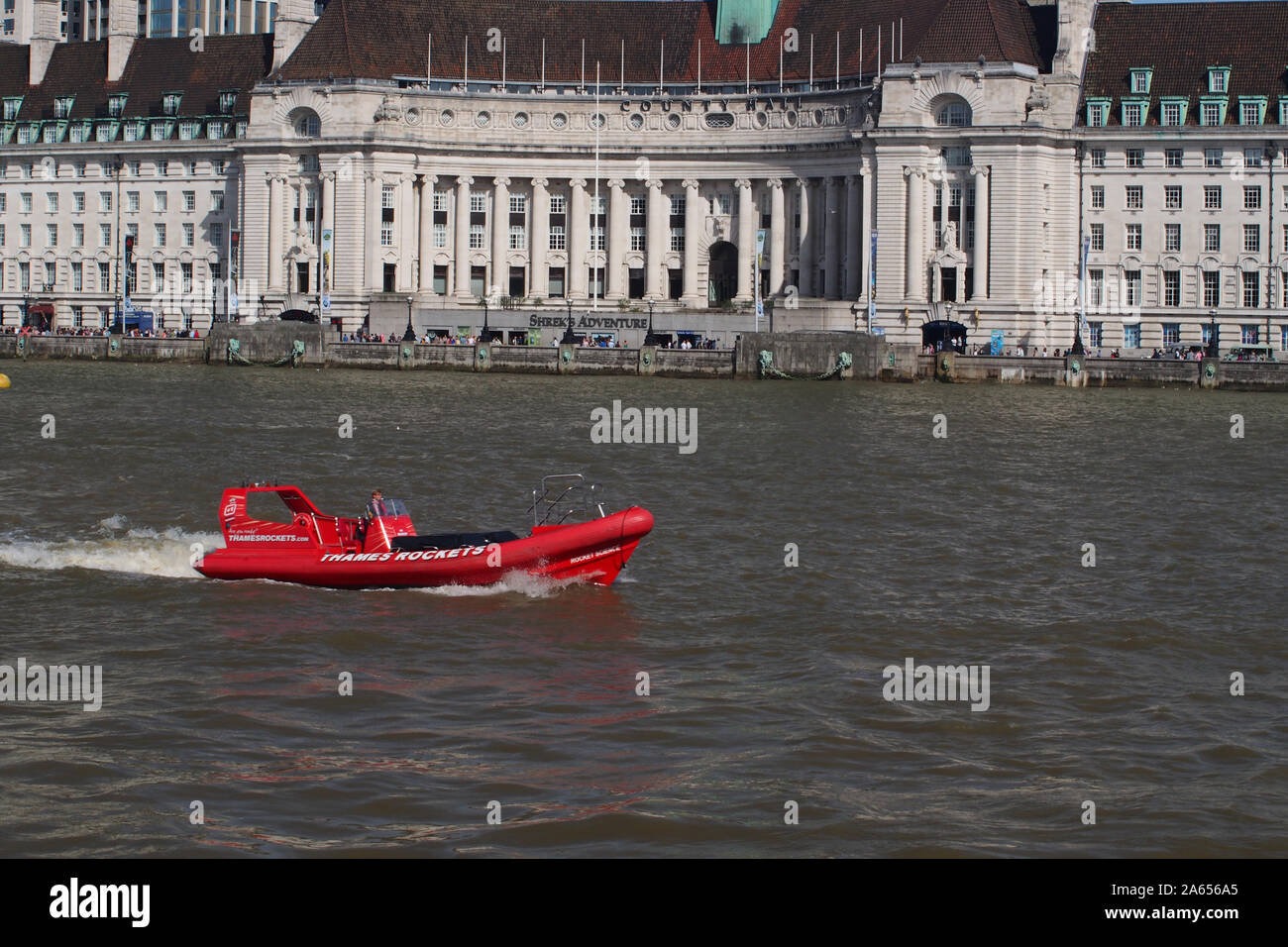 A red speed boat traveling upstream on the River Thames at Westminster ...